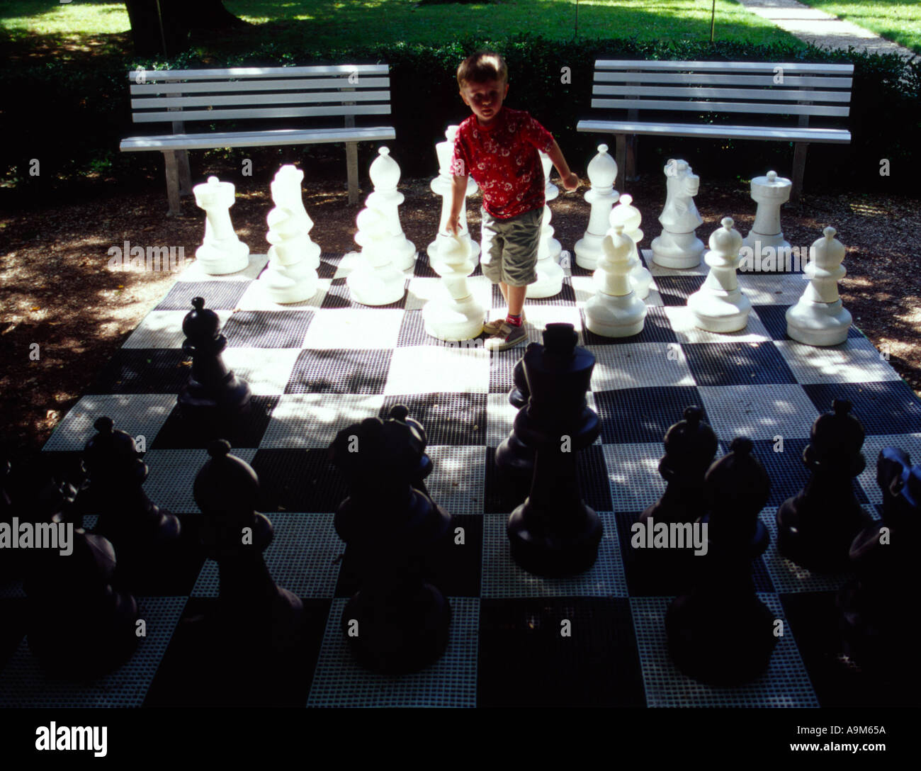 young child playing with chess pieces in park on large chess board ...