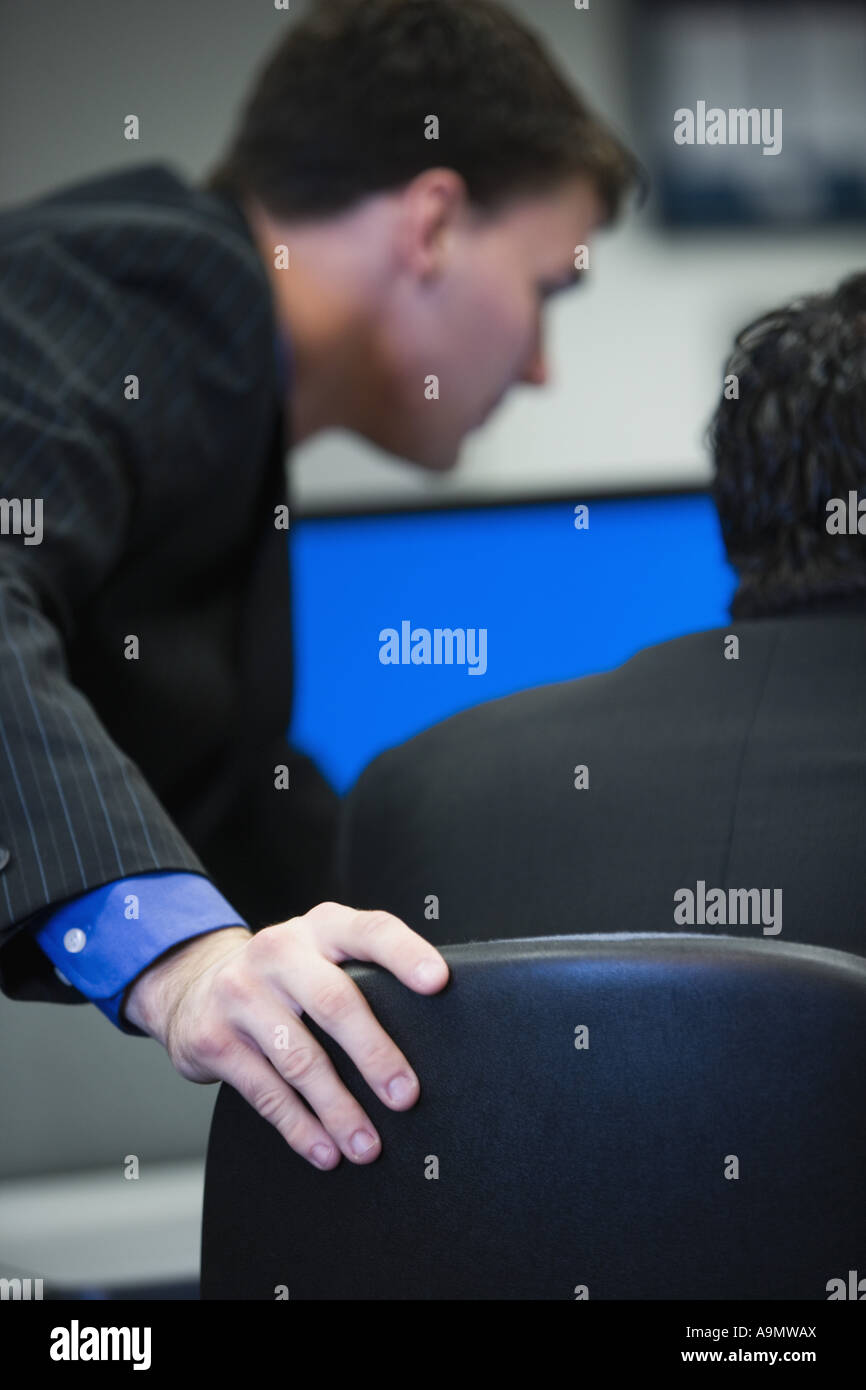 Business man with hand resting on back of chair leaning over computer ...