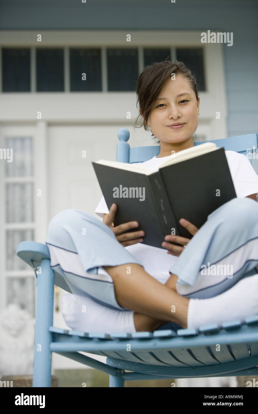 Portrait of pretty young Asian woman sitting on rocking chair reading a ...