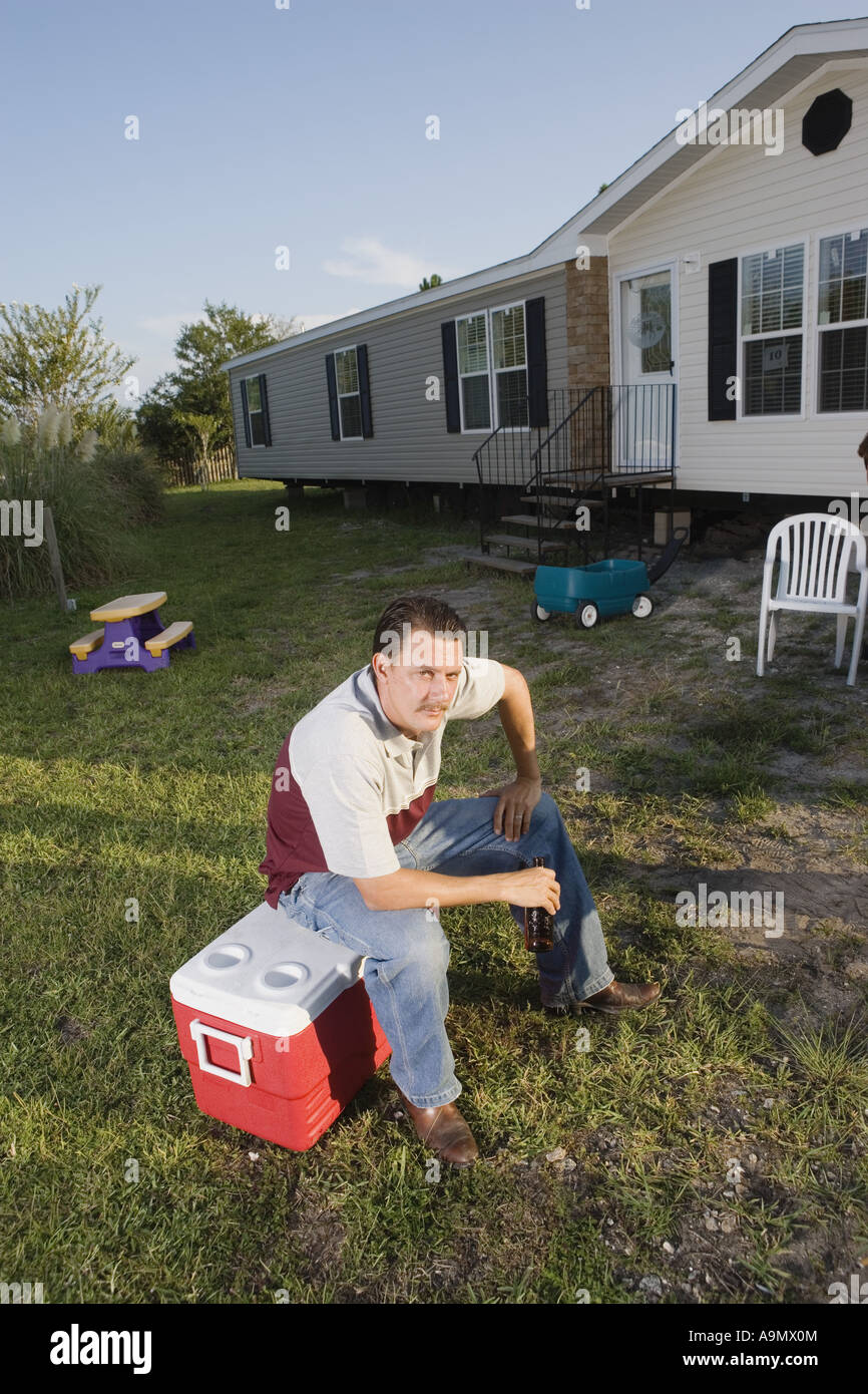 Man sitting on an ice chest holding a drink bottle in front of trailer ...