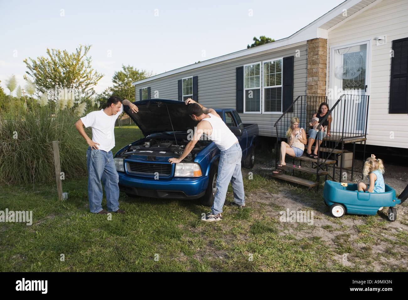 Two men looking under the hood of a pickup truck in front of trailer ...