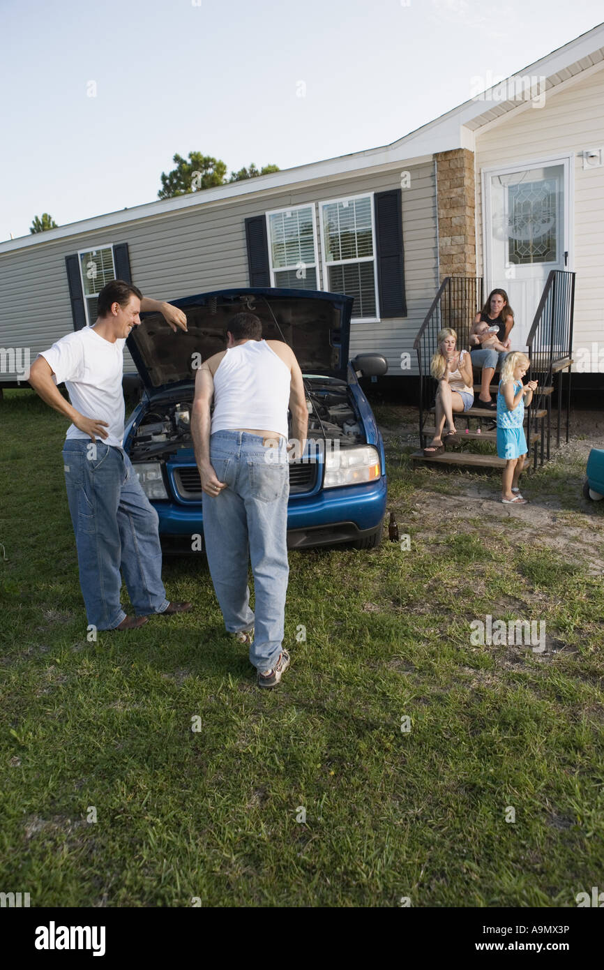 Two men looking under the hood of a pickup truck in front of trailer ...