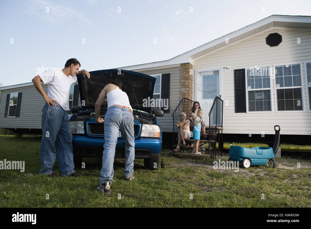 Two men looking under the hood of a pickup truck in front of trailer ...