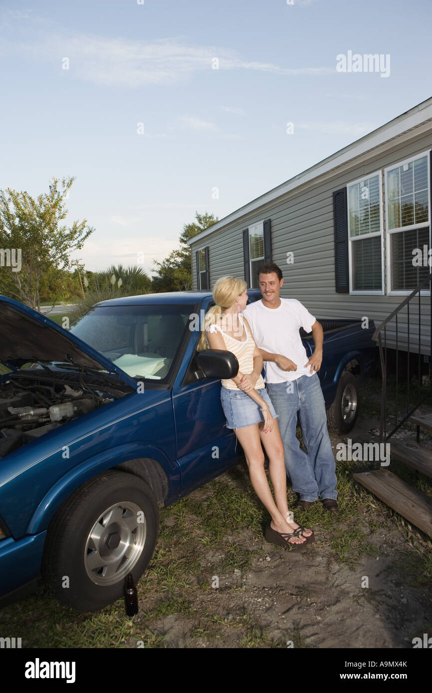 Young couple leaning against old pickup truck in front of trailer home ...