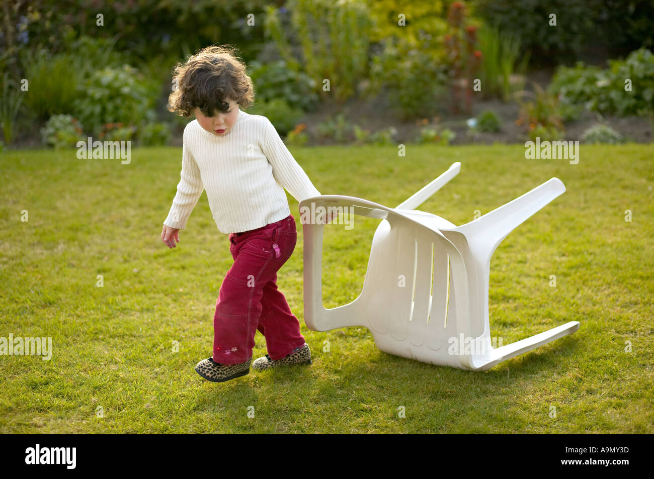 young girl drags plastic garden chair across lawn Stock Photo - Alamy