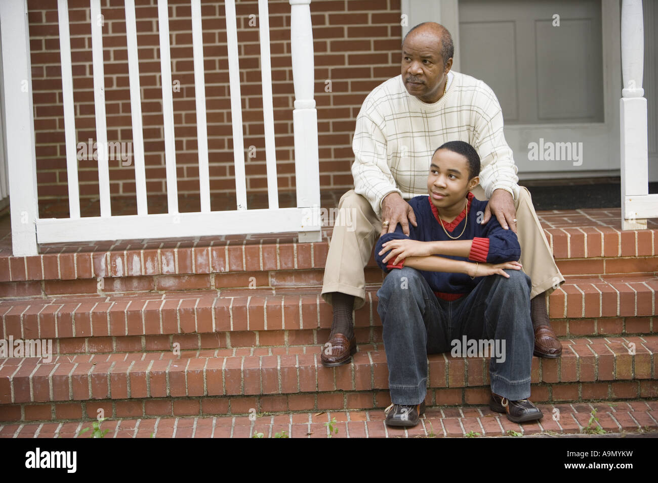 Portrait of a father and teenage son sitting on front porch of house ...