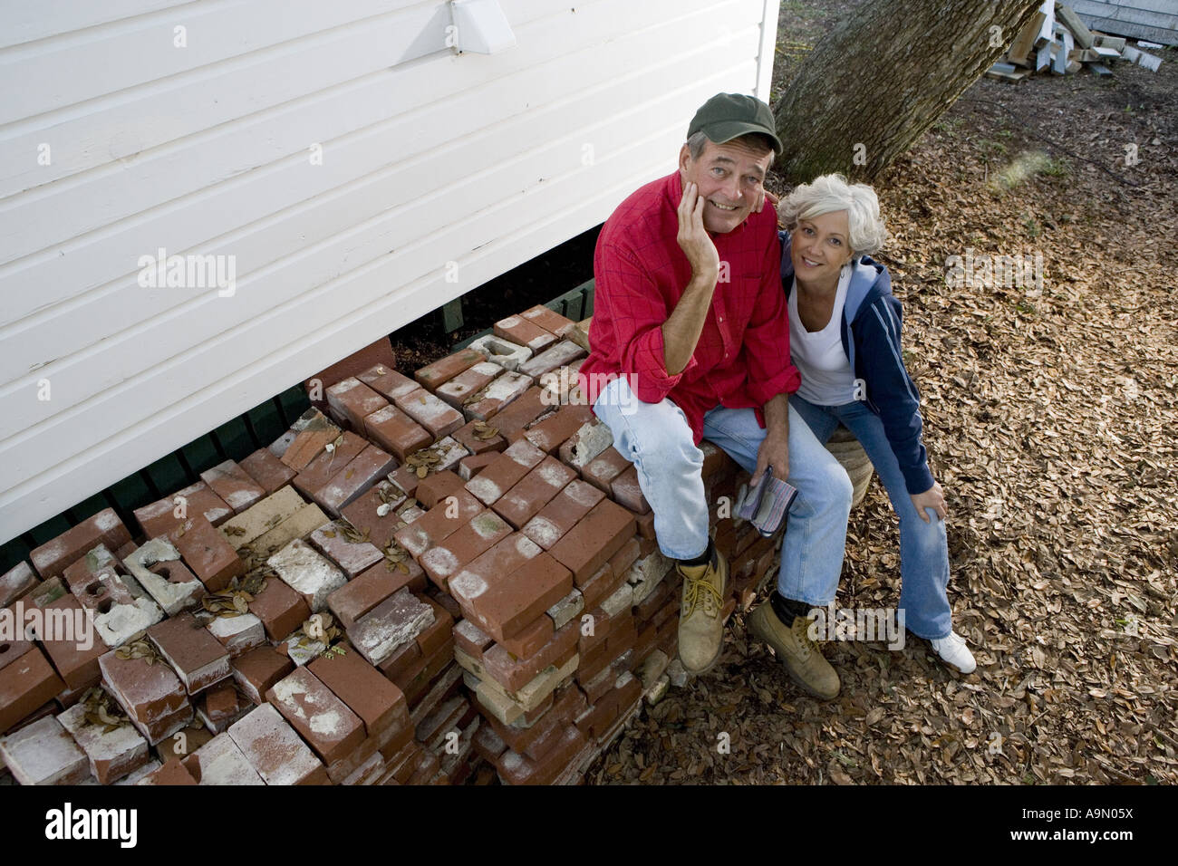 Elevated view of mature couple sitting on stack of bricks outside house ...
