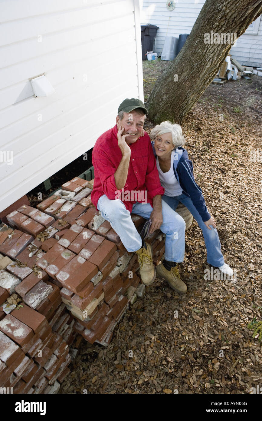 Elevated view of mature couple sitting on stack of bricks outside house ...