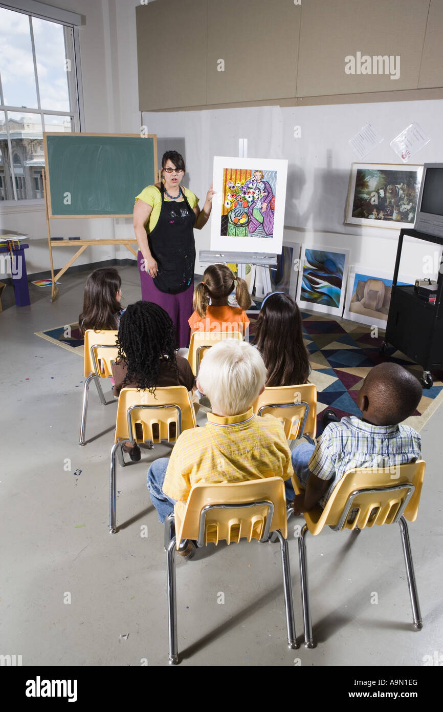 An art teacher standing by easel teaching her young students in art ...