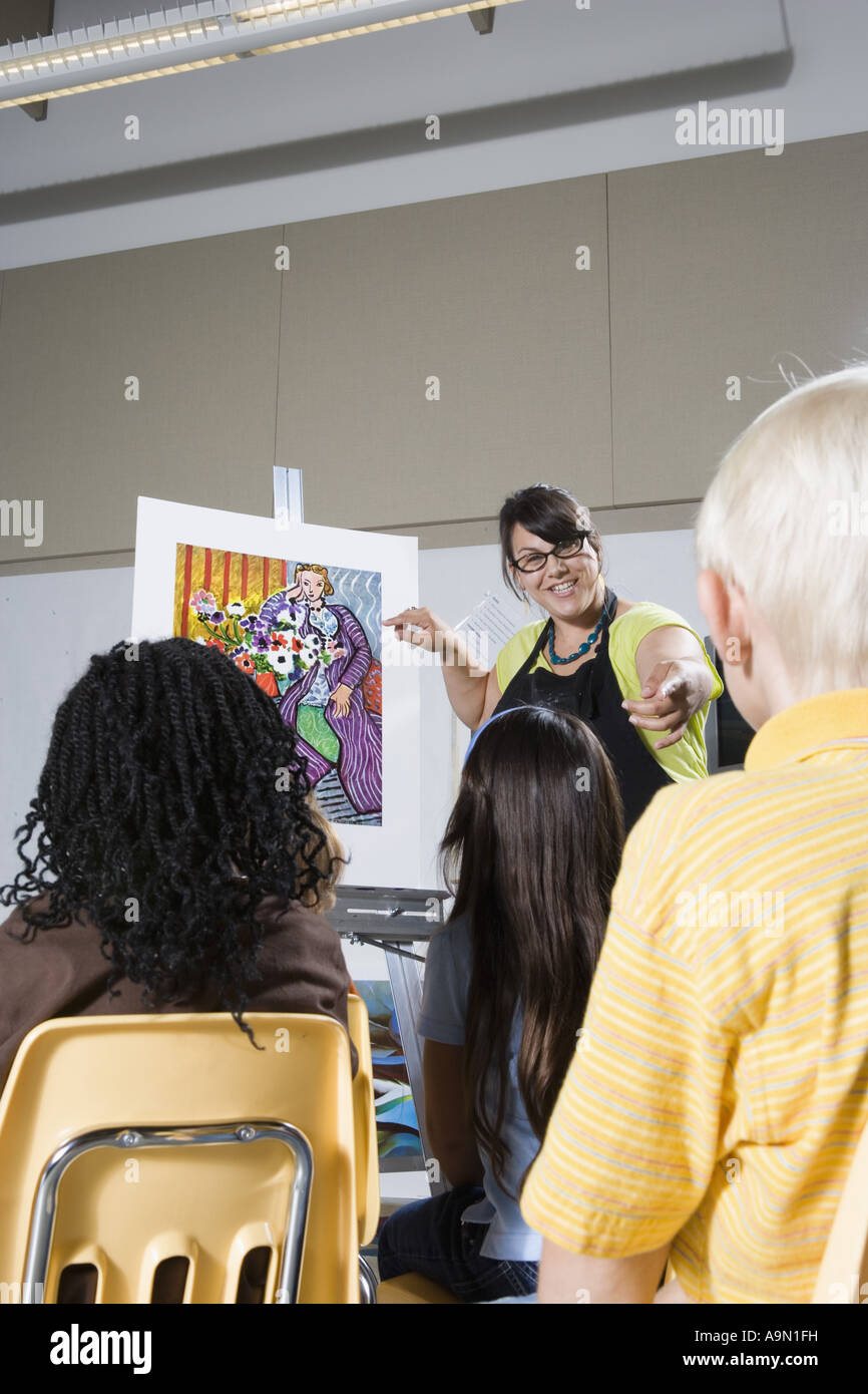 An art teacher standing by easel teaching her young students in art ...