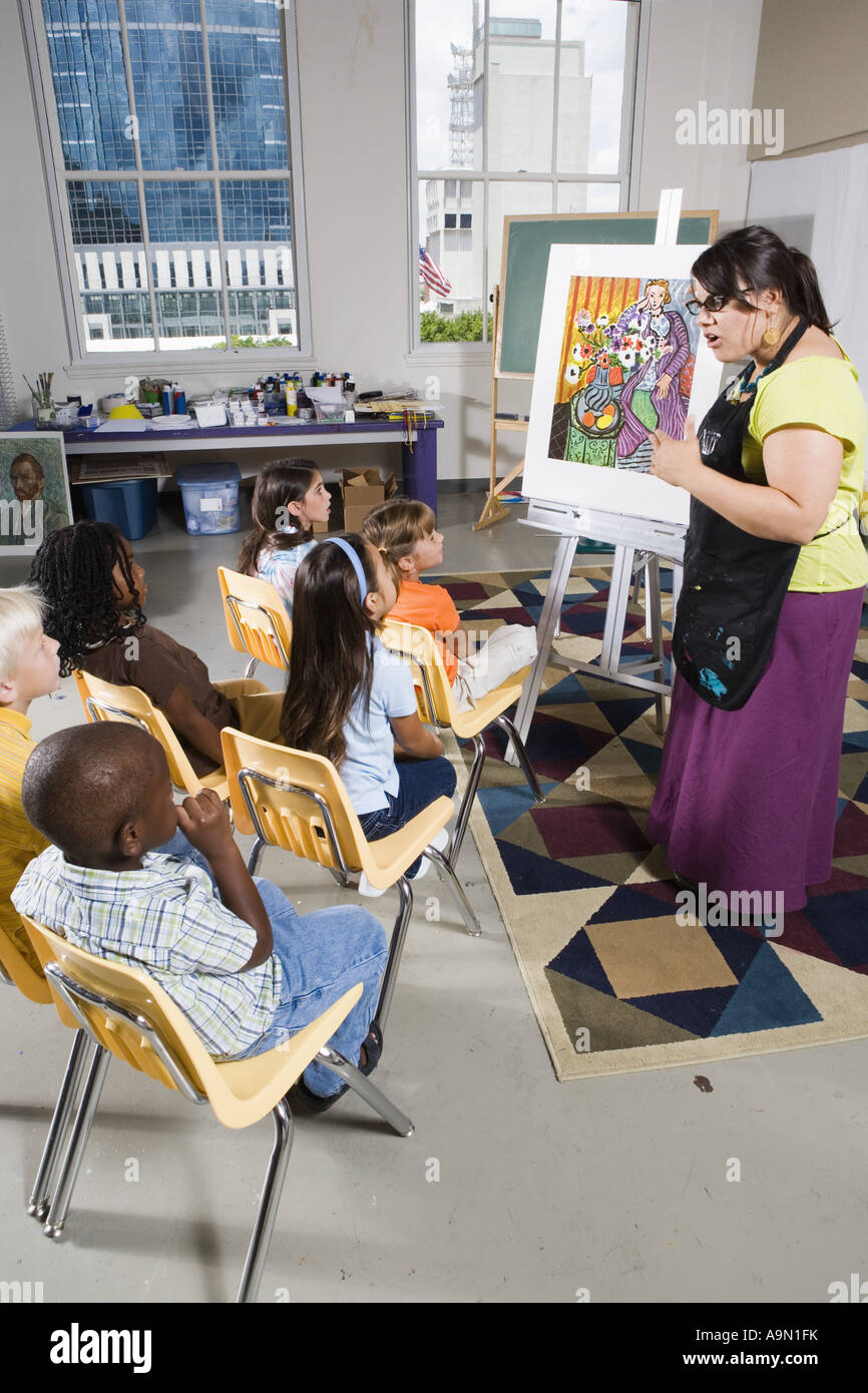 An art teacher standing by easel teaching her young students in art ...