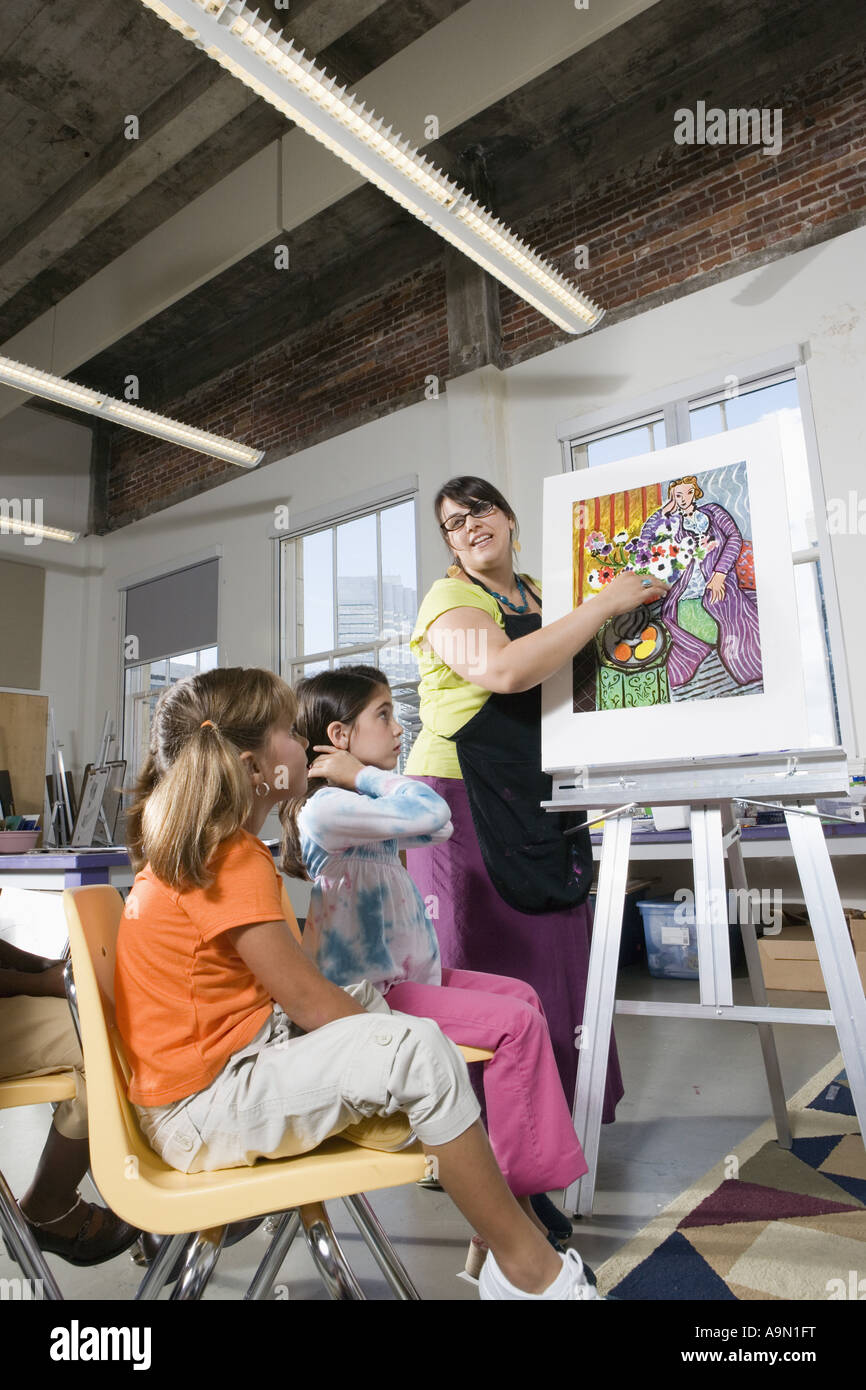 An art teacher standing by easel teaching her young students in art ...