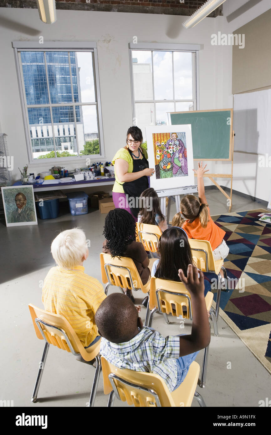 An art teacher standing by easel teaching her young students in art ...