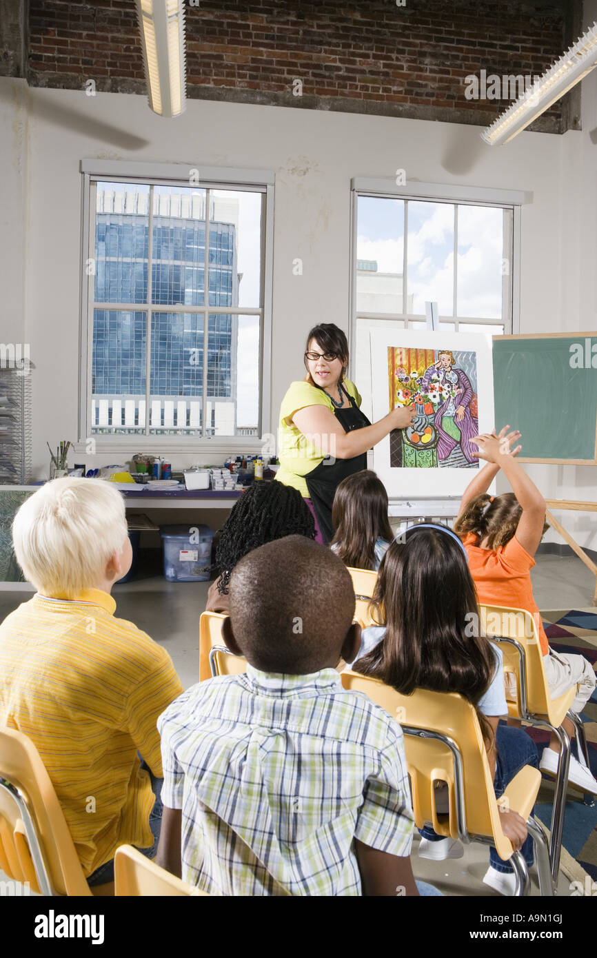 An art teacher standing by easel teaching her young students in art ...