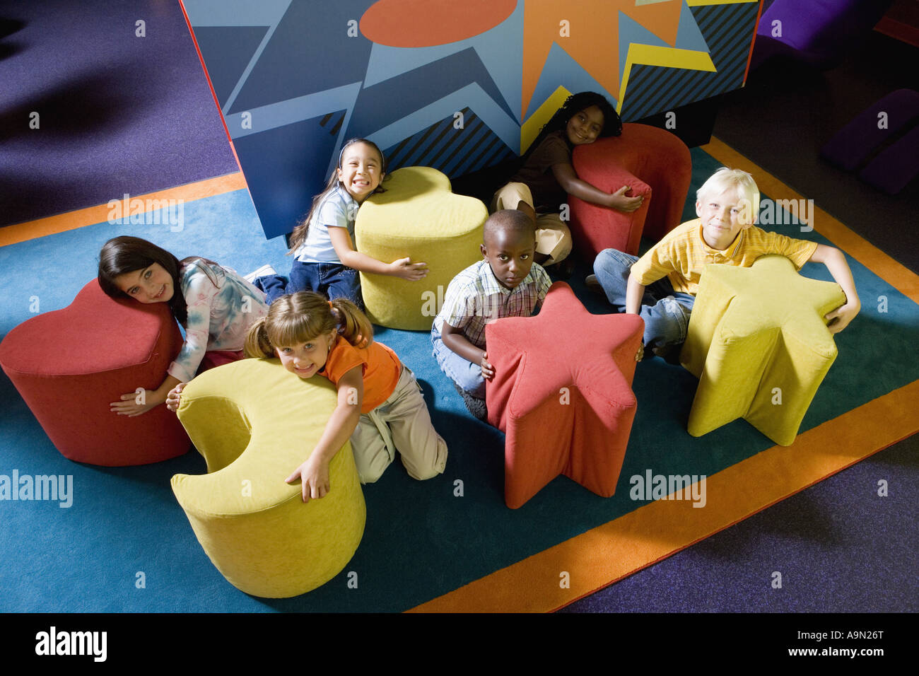 Elevated view of children hugging colorful seats of various shapes ...