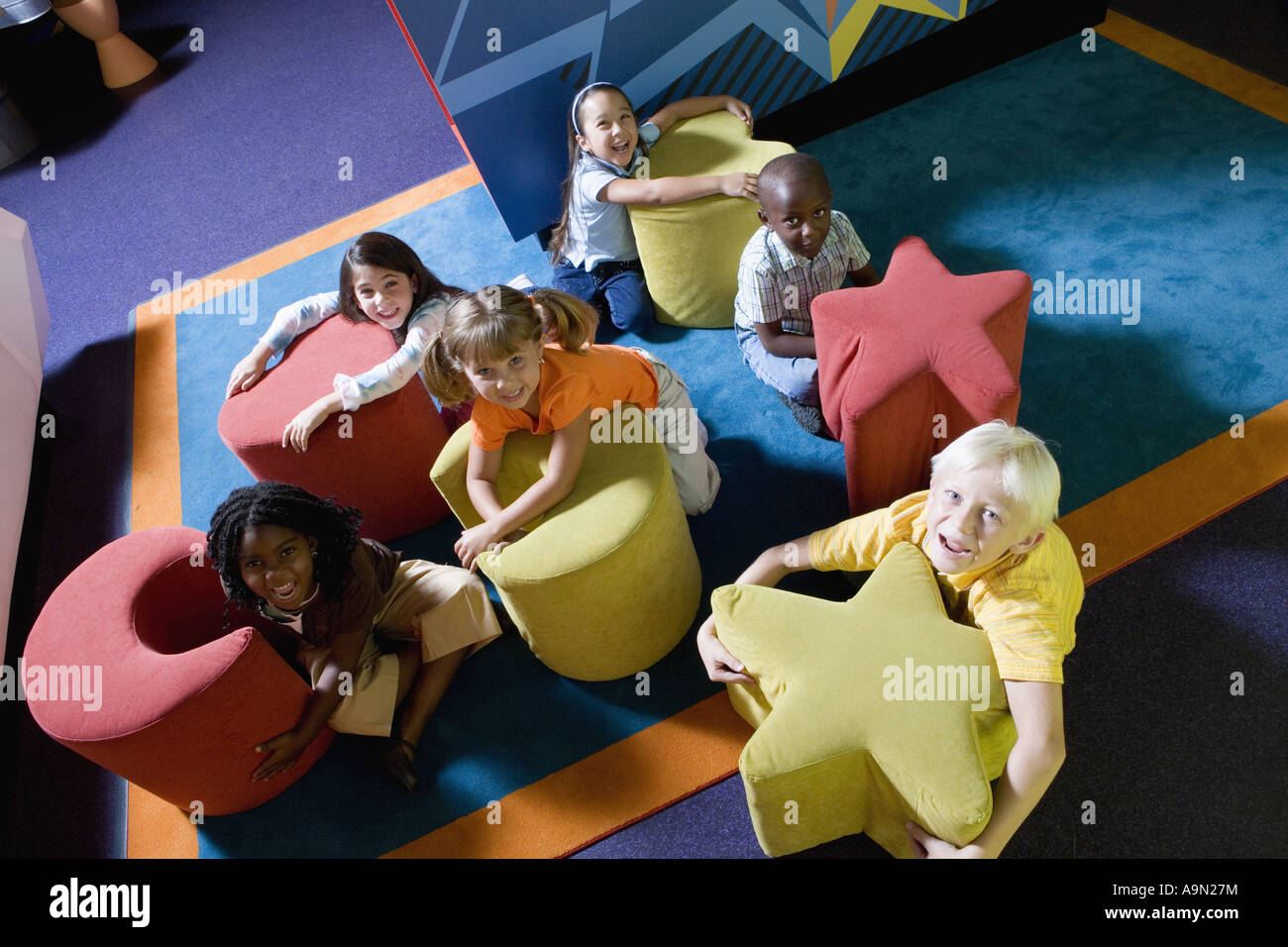 Elevated view of children hugging colorful seats of various shapes ...