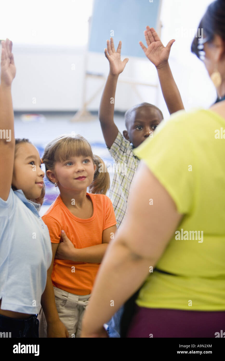 Teacher with her young students raising hands Stock Photo - Alamy