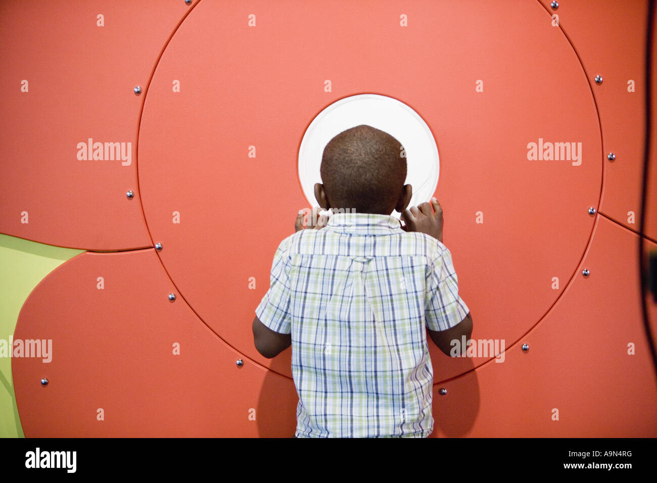 Boy (5-6) looking through opening in a colorful wall Stock Photo - Alamy