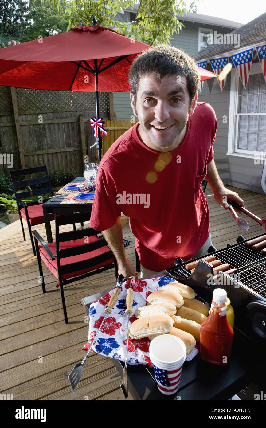 Man grilling hot dogs in backyard patio with picnic table and 4th of ...