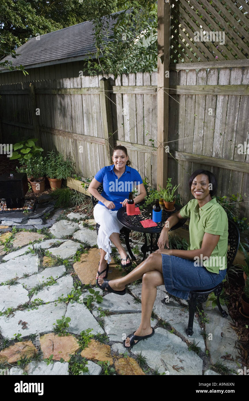 Two women sitting together around backyard patio table with cold ...