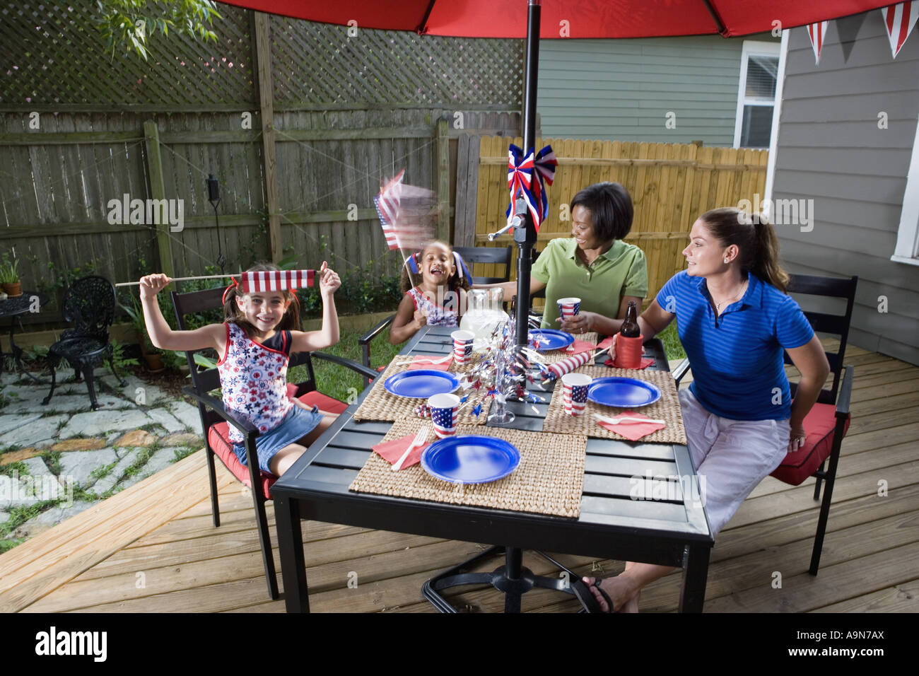 Two young girls with moms at 4th of July cookout waving American flags ...