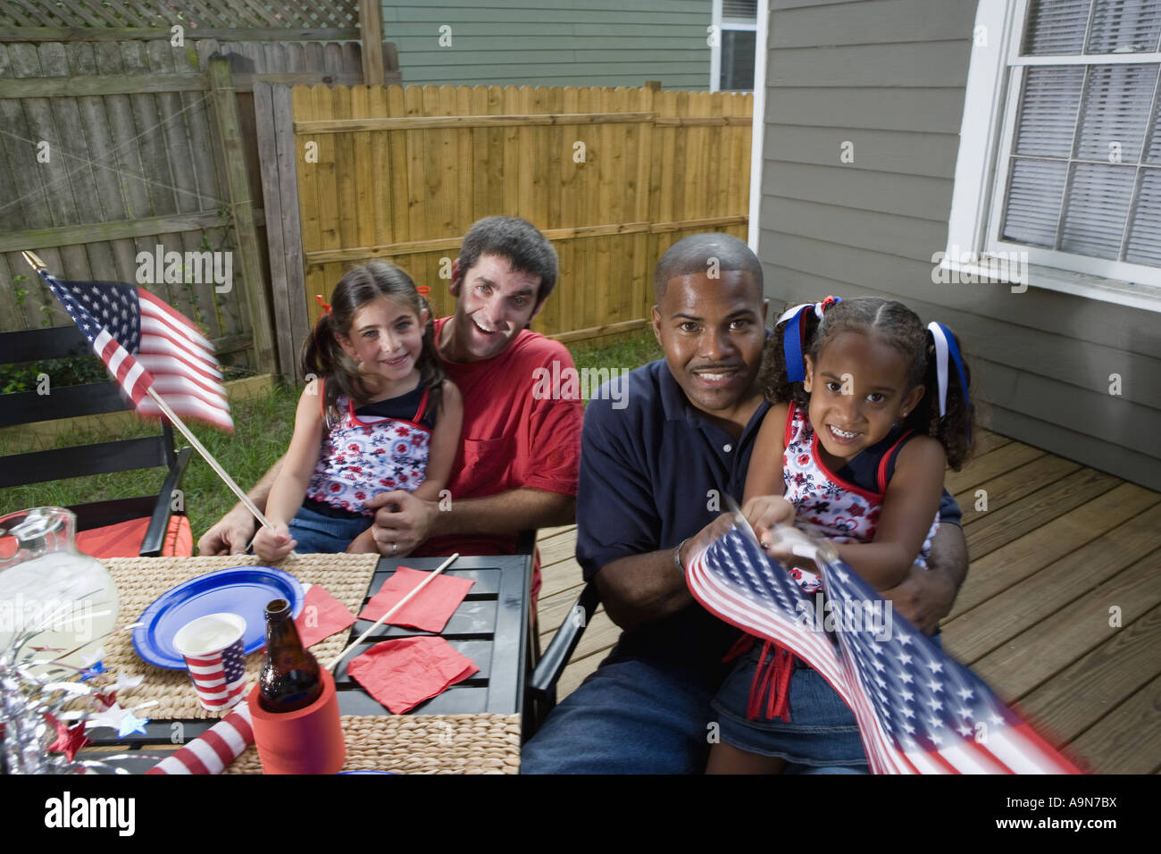 Two young girls with dads at 4th of July cookout waving American flags ...