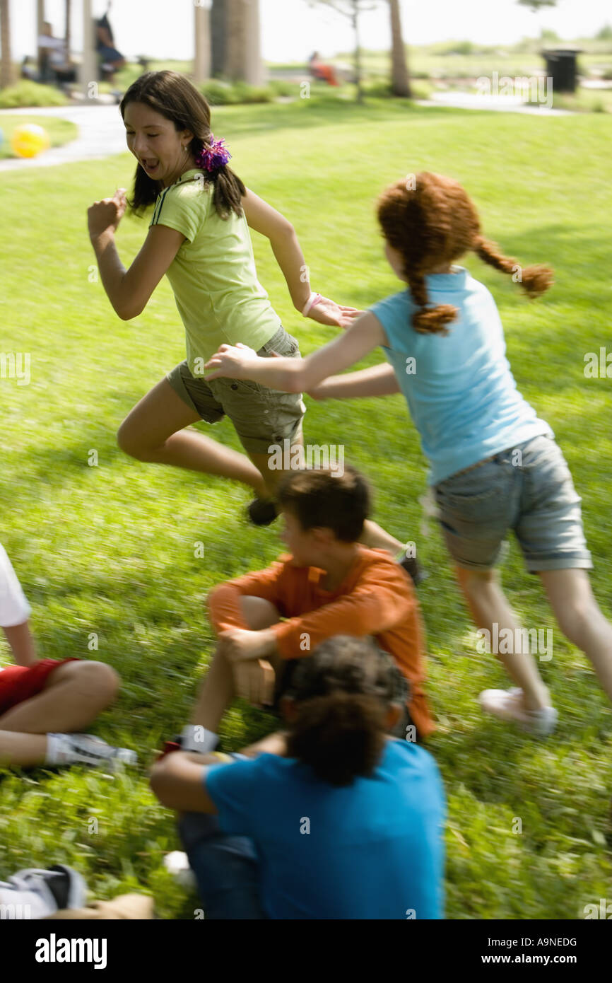 Two girls running around children sitting in a circle on the grass ...