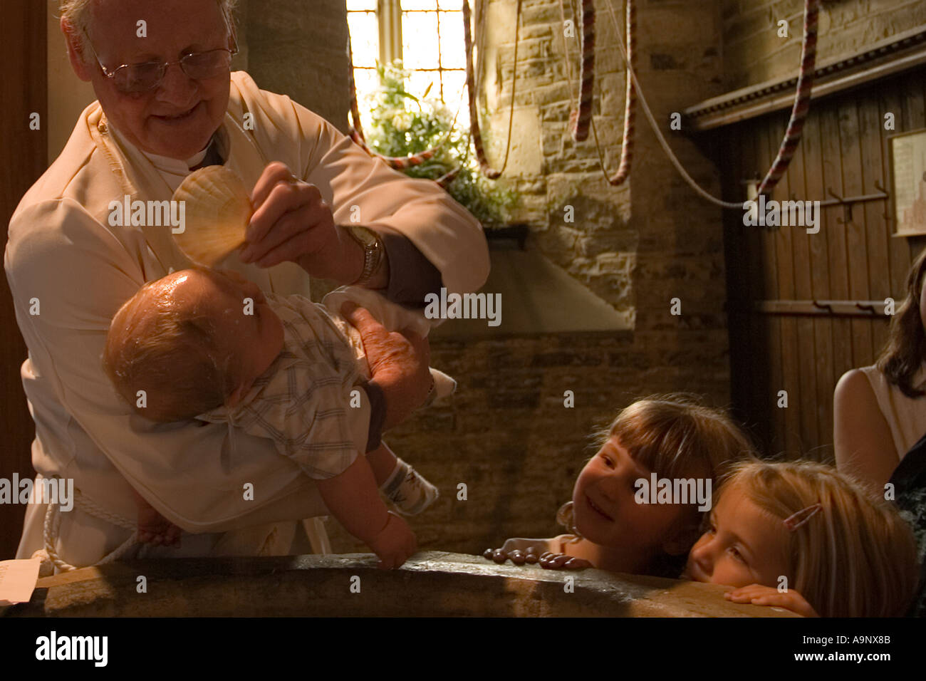 Two little girls peer over the font as a priest Christens a baby boy ...