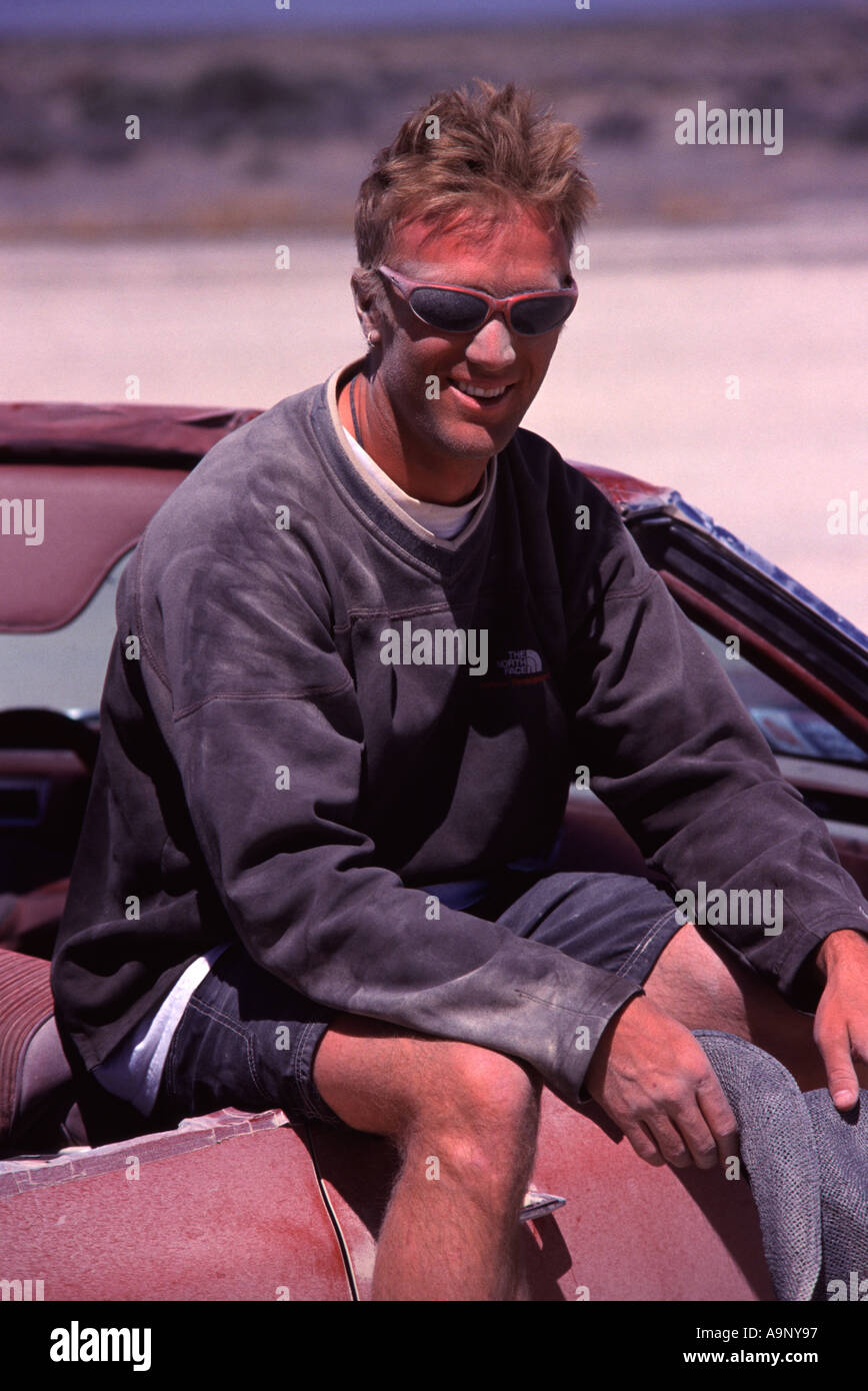 A dusty man sitting on a dusty car after driving across a dry lake bed ...