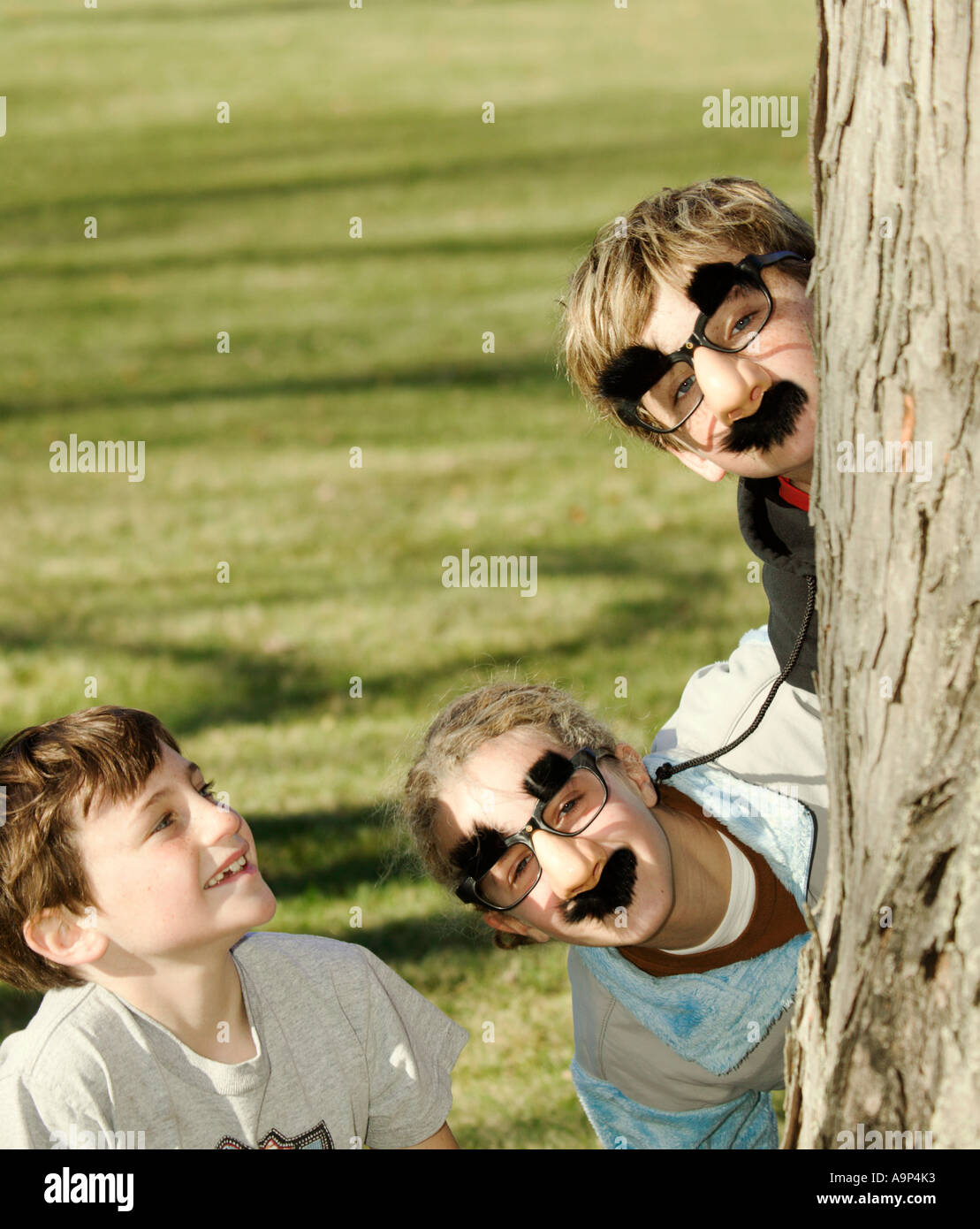 Kids hiding behind tree with silly disguises Stock Photo - Alamy