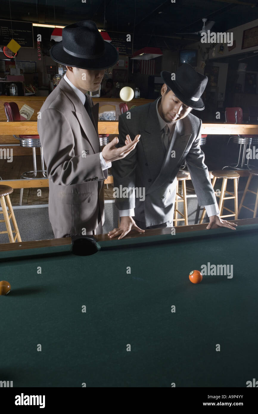 View of two men in suits and hats standing beside billiards table and ...