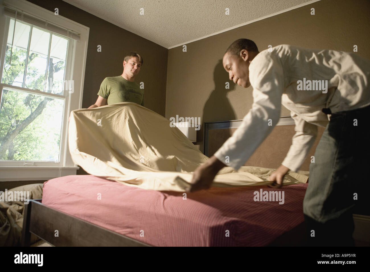 Two young men making a bed Stock Photo - Alamy