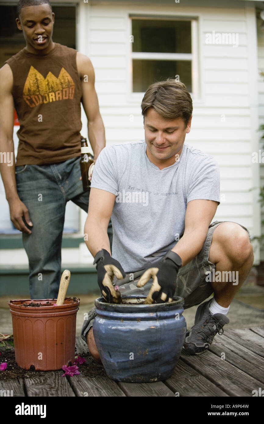 Young man moving plant to a new planter, friend watching Stock Photo ...