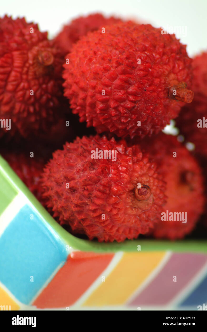Red lichees in multi coloured dish on white background Stock Photo - Alamy