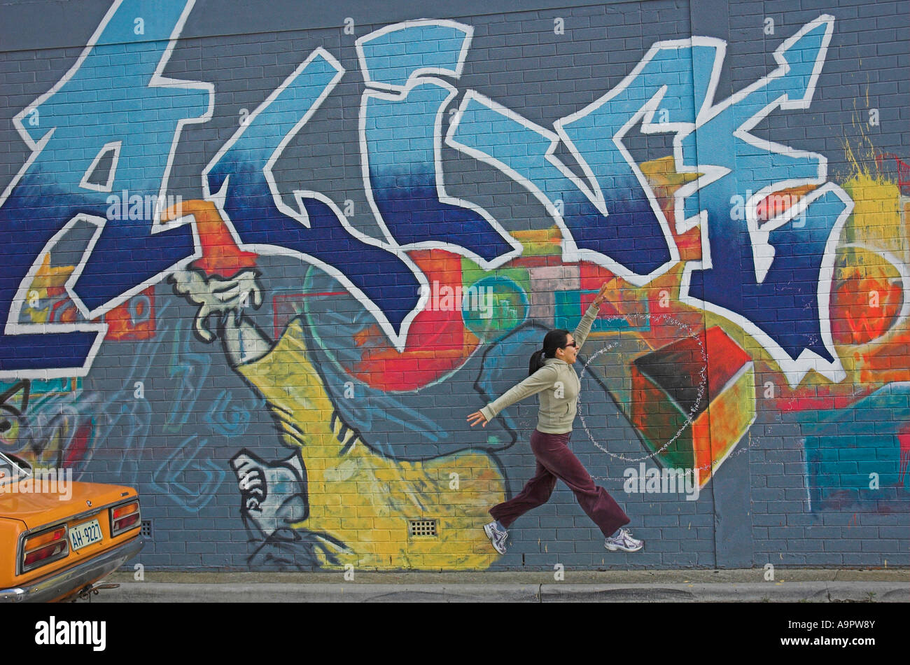 Young woman jumps in front of graffiti painted wall Stock Photo - Alamy