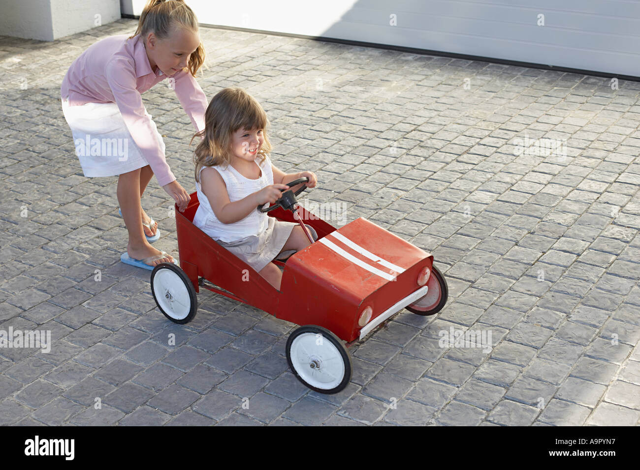 Sister pushing her younger sister in a toy car Stock Photo - Alamy