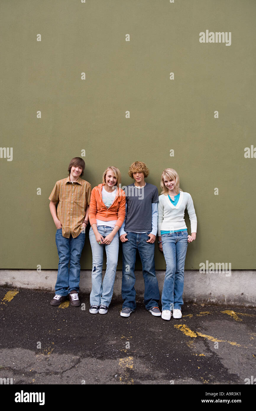 Four teenagers leaning against a wall Stock Photo - Alamy