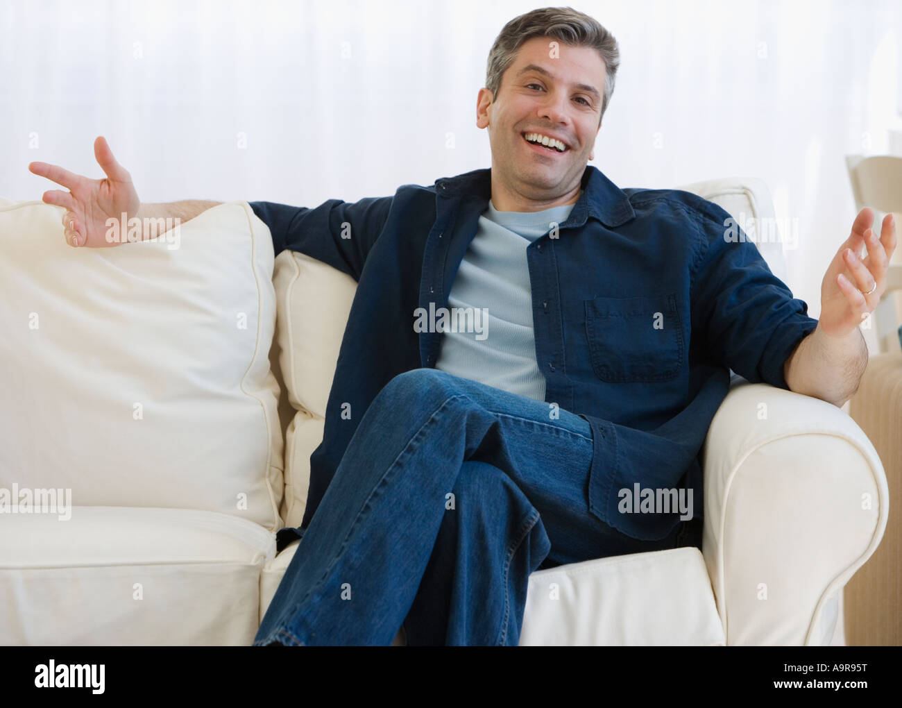 Man shrugging shoulders on sofa Stock Photo - Alamy