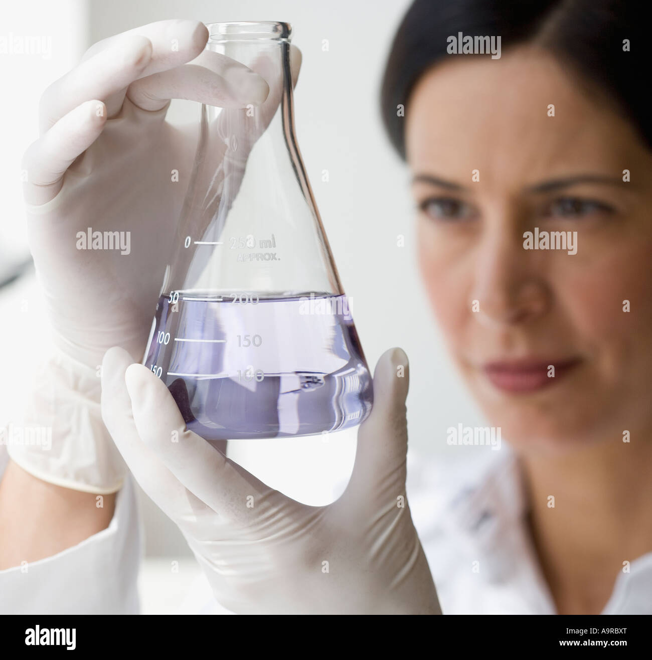 Female scientist looking at liquid in beaker Stock Photo - Alamy