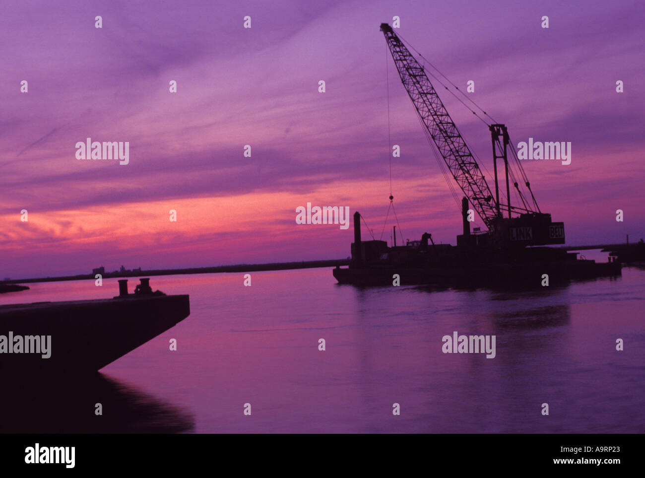 Construction crane sitting in small harbor silhouetted by purple and ...