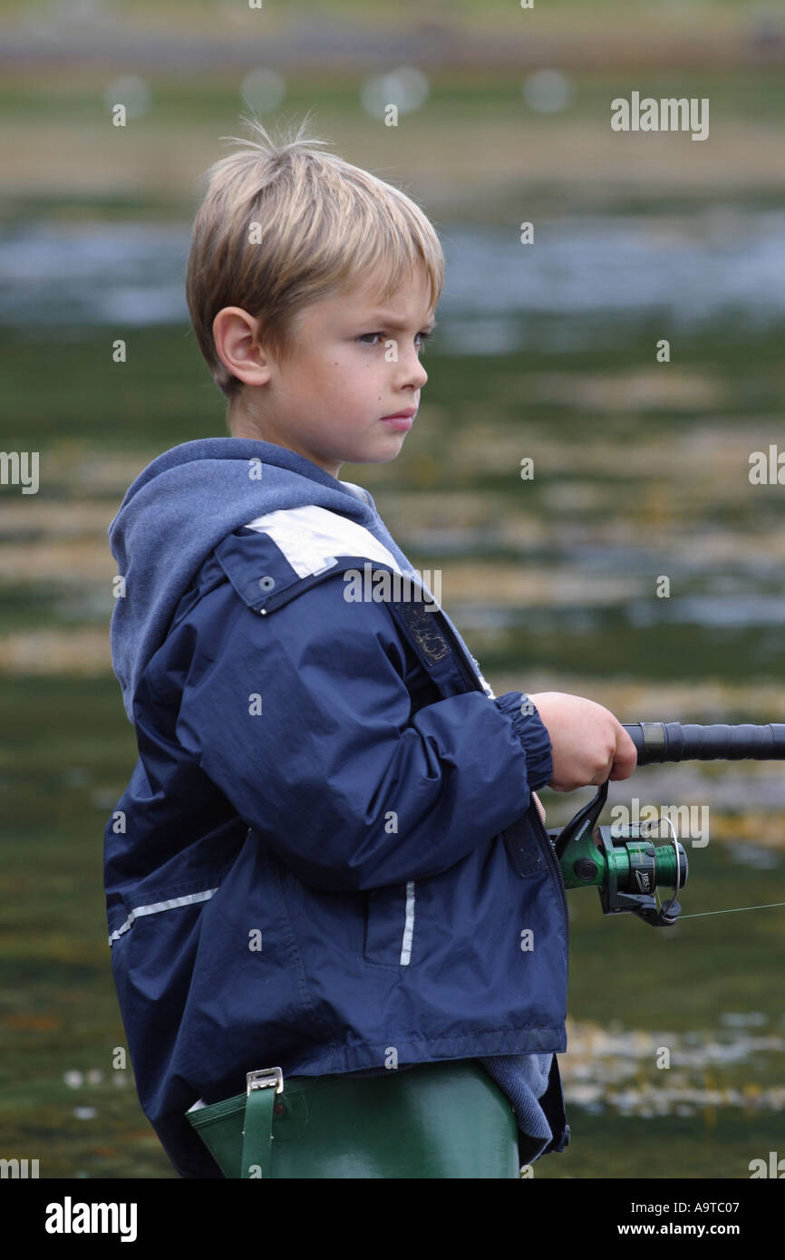 Young boy fishing with rod and reel in a Scottish loch wearing wadders ...