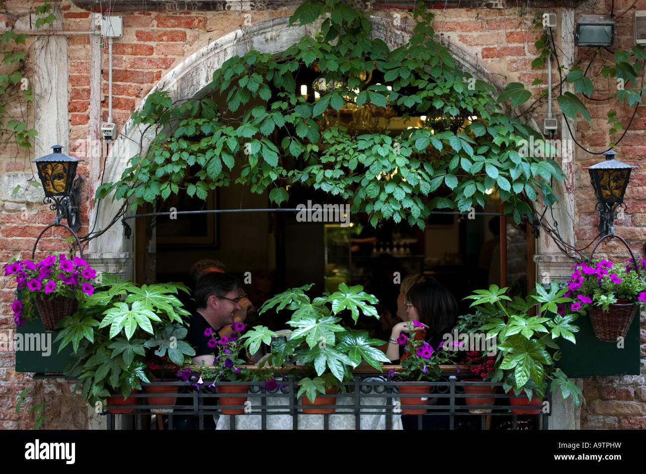Open window of restaurant with diners surrounded by plants and flowers ...