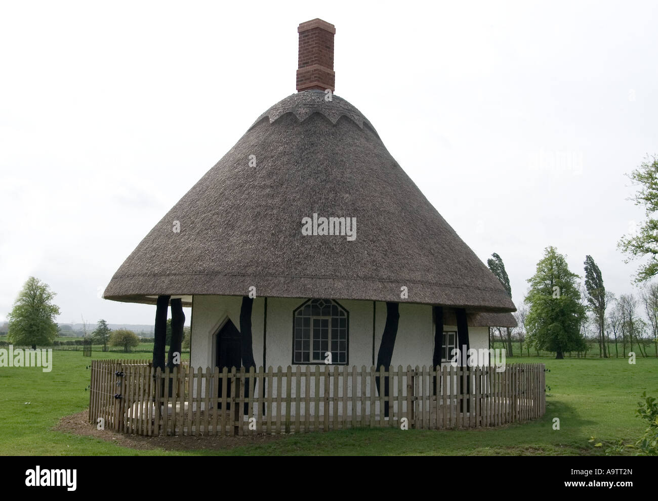 thatched round white cottage with picket fence around it Stock Photo ...