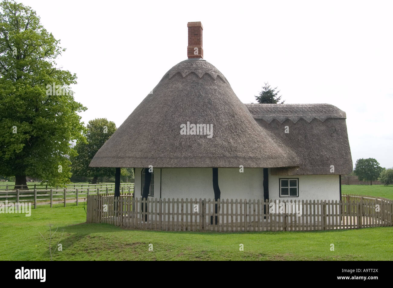thatched round white cottage with picket fence around it Stock Photo ...