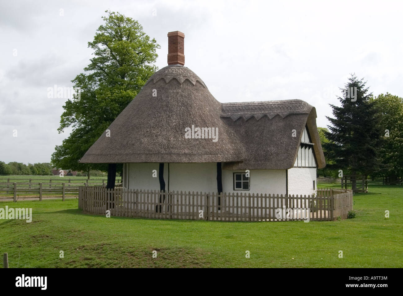 thatched round white cottage with picket fence around it Stock Photo ...