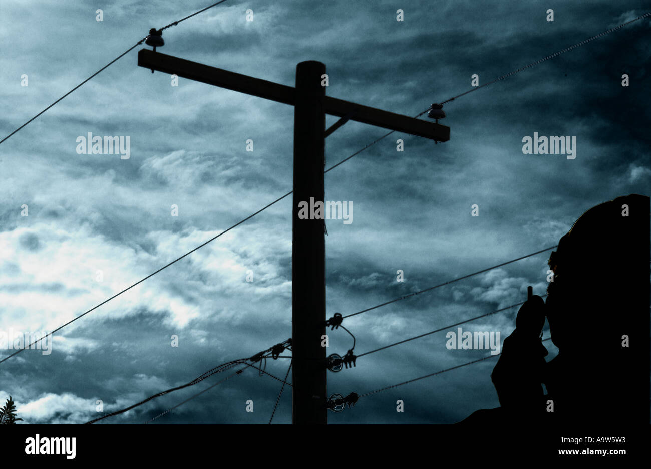 electrician and electric power lines silhouetted against stormy sky in ...