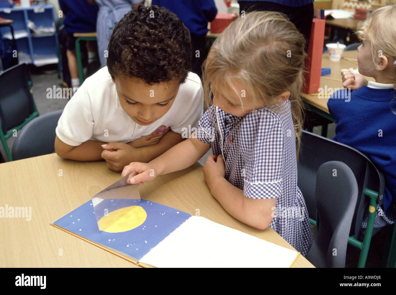 Primary classroom children examining a book with a mirror Stock Photo ...