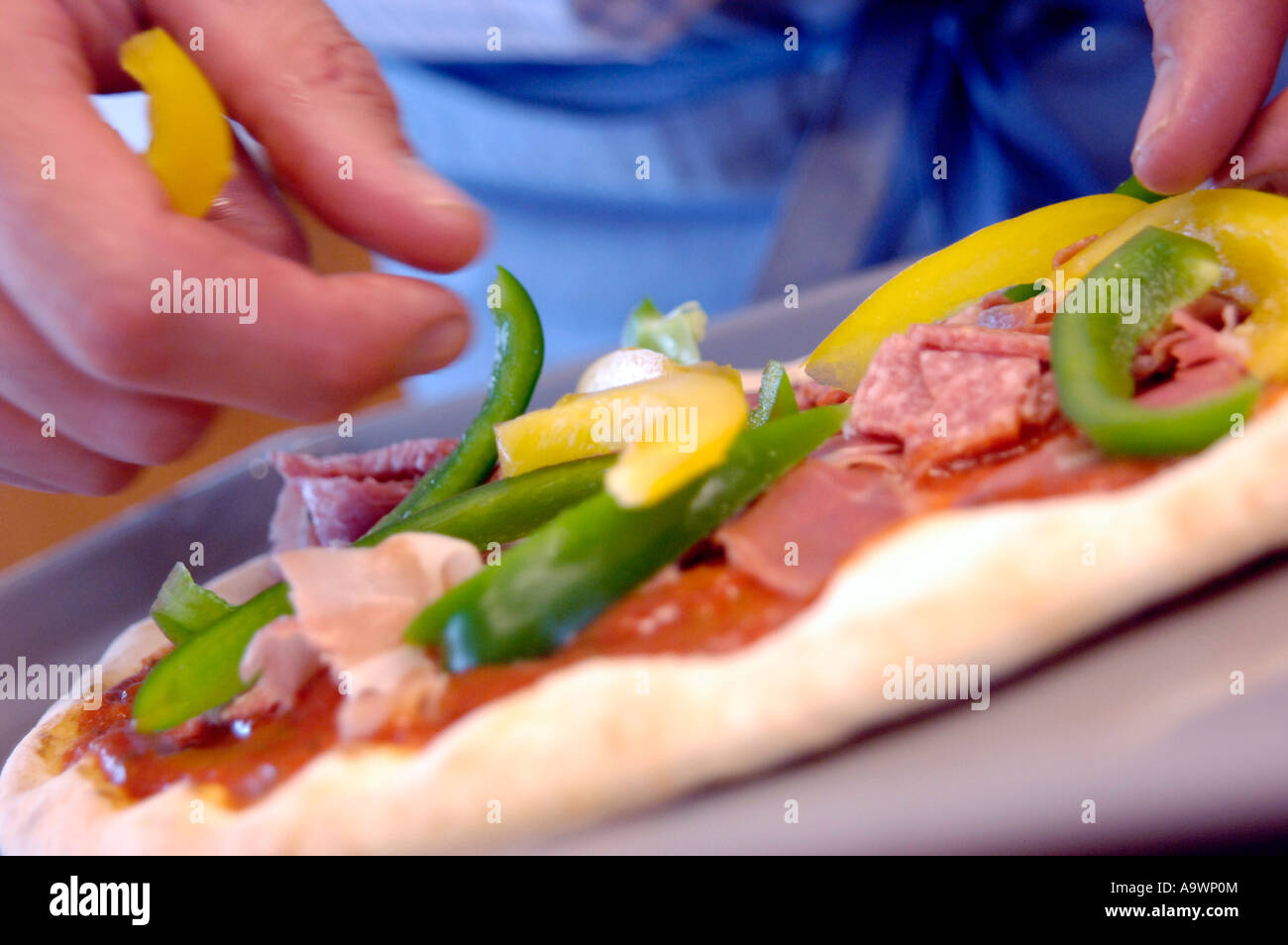Adding sliced peppers ham and salami to a pizza base Stock Photo - Alamy