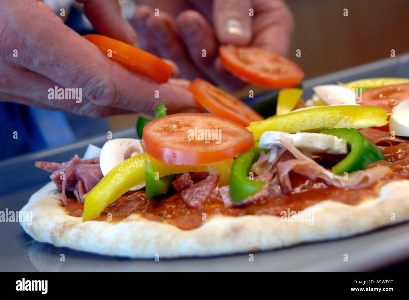 Adding sliced tomatoes peppers ham and salami to a pizza base Stock ...