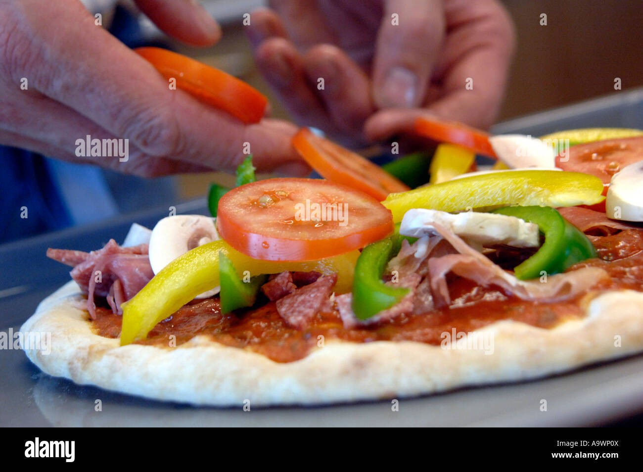 Adding sliced tomatoes peppers ham and salami to a pizza base Stock ...